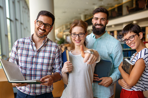 Happy university students studying with books in library. Group of ...