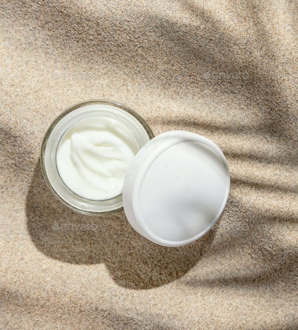 Opened Cream jar with white lid on beige sand top view, palm leaf ...