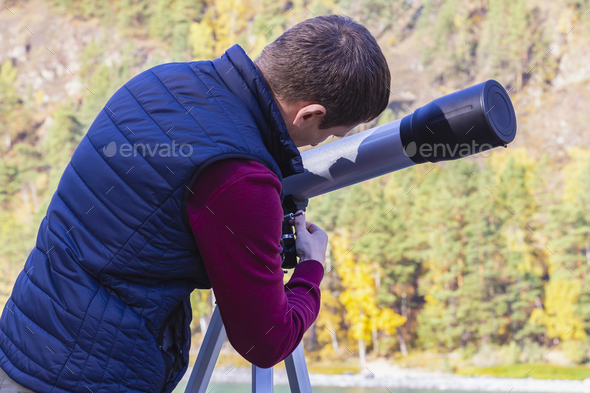 Man sets up telescope on tripod to survey mountains, autumn landscape ...