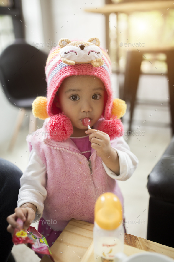 A portrait of a cute little girl in a pink dress eating a bright red ...