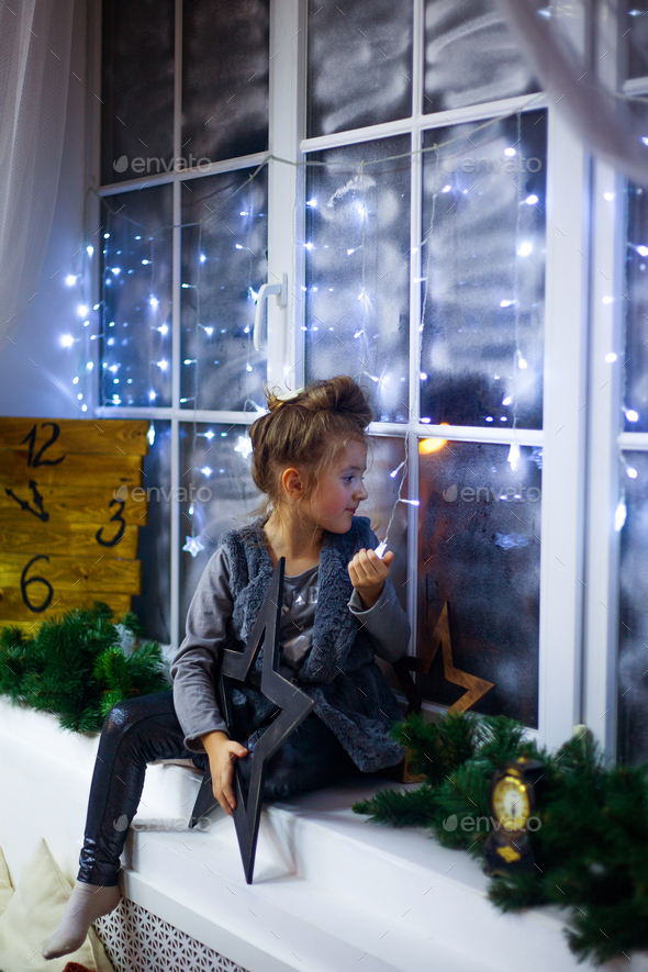 Cute little girl sitting by the window and waiting for Holiday Stock ...