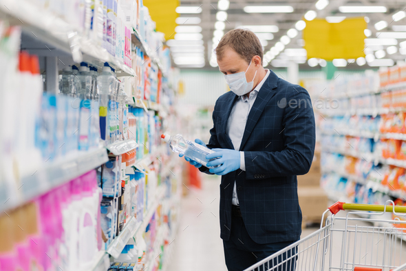 man chooses detergent in housekeeping store, reads label and ...
