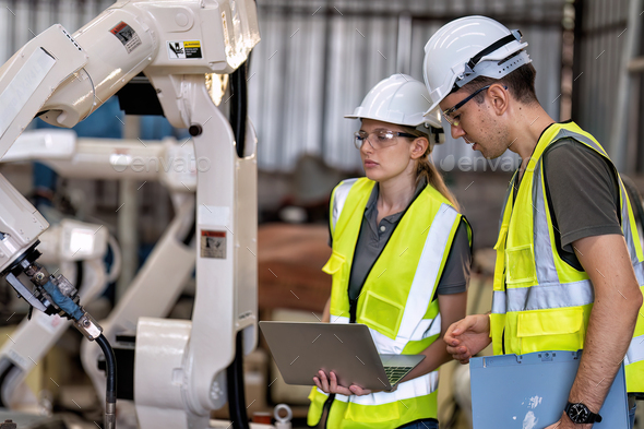 In robotic training instructor teach girl engineer to program robot arm look manual from laptop ...