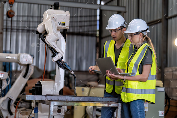 In robotic training instructor teach girl engineer to program robot arm look manual from laptop ...
