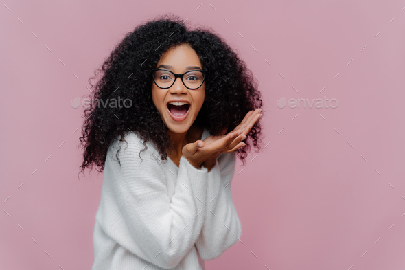 Overjoyed happy curly young woman with cheerful expression, keeps mouth ...