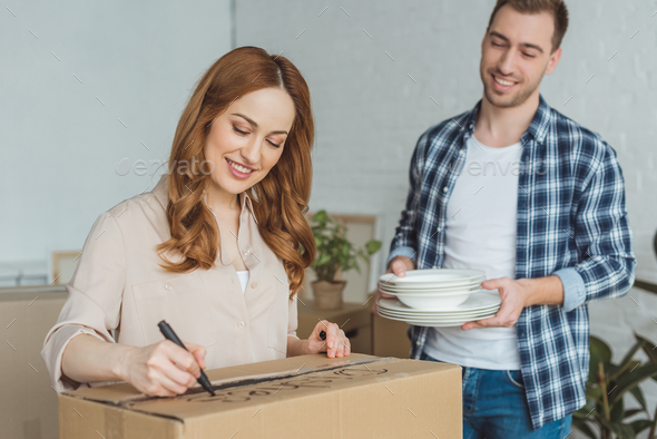 smiling woman signing cardboard box with husband with dishes near by ...