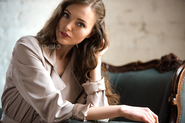 elegant brunette woman in trench coat sitting in armchair Stock Photo ...