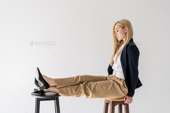 side view of beautiful fashionable blonde girl sitting on stool and ...