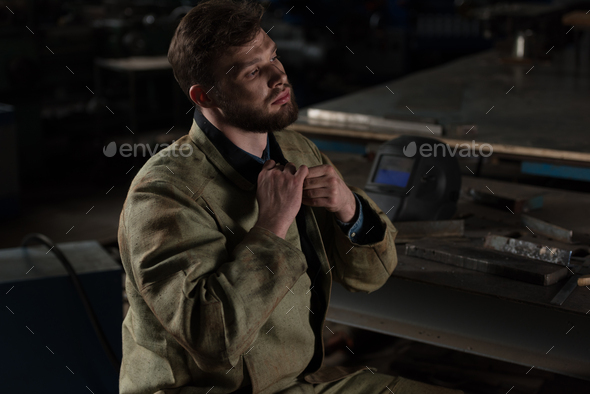 young male worker buttoning up his uniform at factory Stock Photo by ...