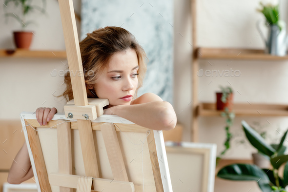 beautiful sensual young woman leaning at easel and looking away in art studio Stock Photo by ...