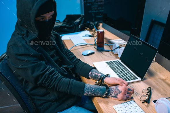 busted hacker in mask with handcuffs in front of workplace Stock Photo ...