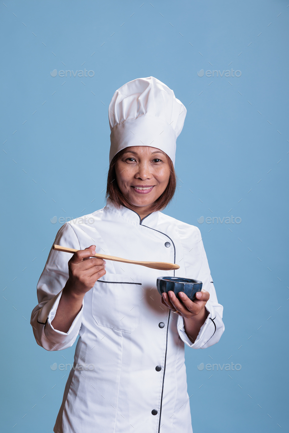 Professional smiling cook holding kitchen bowl tasting prepared food ...