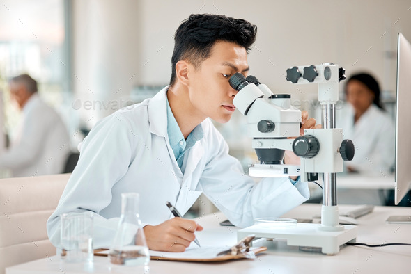 Shot of a young scientist writing notes while using a microscope in a ...
