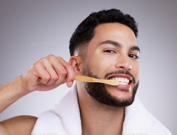 Shot of a handsome young man brushing his teeth against a studio ...