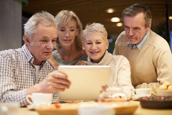 Elderly former classmates watching old photos on tablet Stock Photo by ...