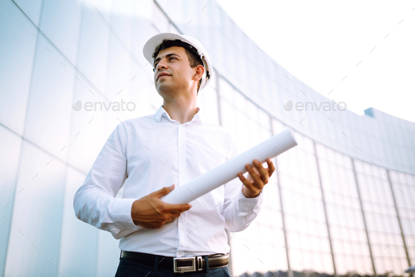 Young worker in a helmet and with a phone at a work object. Business ...
