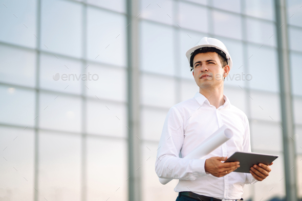 Young worker in a helmet and with a phone at a work object. Business ...