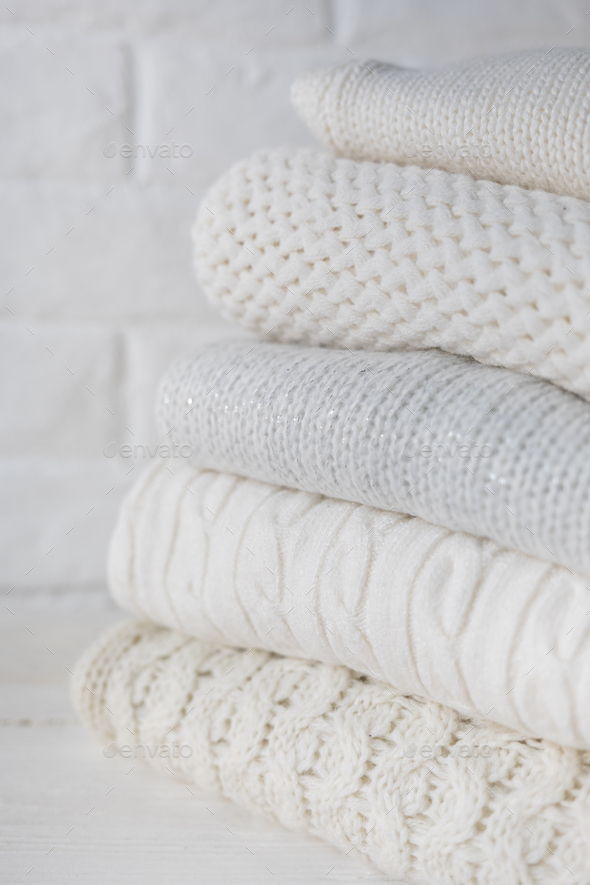 Stack of white cozy knitted sweaters and beads against the background ...