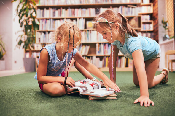 Two schoolgirls reading books in school library. Primary school ...