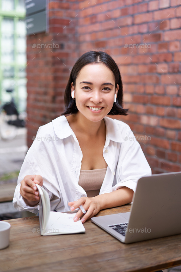 Stylish asian girl works in coworking with laptop, makes notes, uses ...