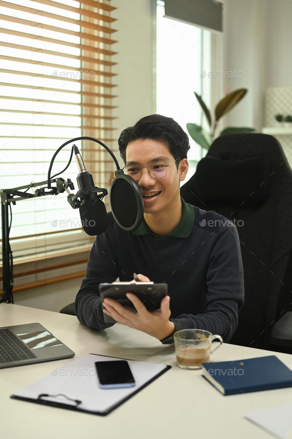 Smiling asian male podcaster sitting front of condenser microphone and ...