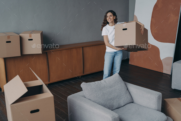 Happy young woman relocates alone and carrying a box. Single spanish ...