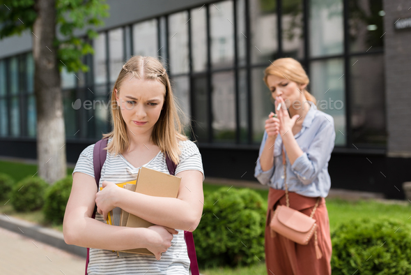 disappointed teen daughter with books looking down while her mother ...