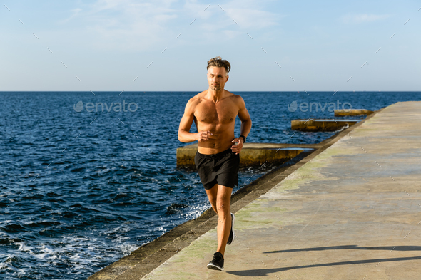 muscular shirtless sportsman jogging on seashore Stock Photo by ...