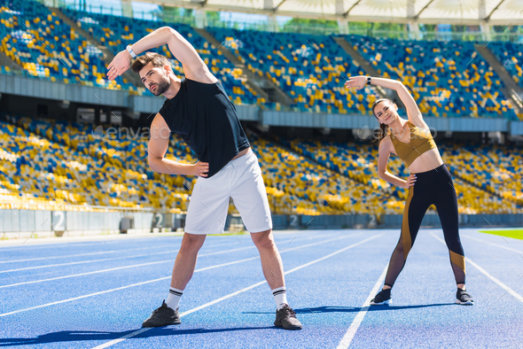 young sportive couple doing side bend before training on running track ...