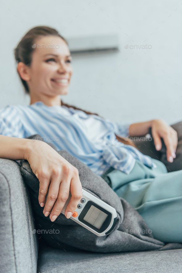 selective focus of woman sitting on sofa with air conditioner remote ...