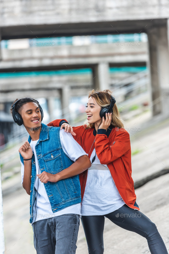 happy multicultural couple listening music with headphones and dancing ...