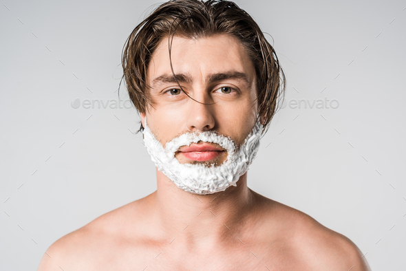 portrait of young man with shaving foam on face looking at camera isolated on grey Stock Photo ...