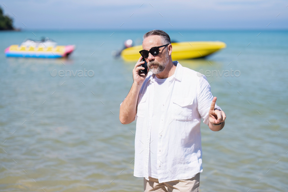 Business man on holiday walk along the beach but continue work use ...