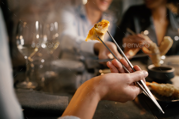 Detail of a woman's hand grabbing a spring roll with metallic ...