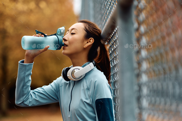 Thirsty Asian female athlete drinking water during sports training ...