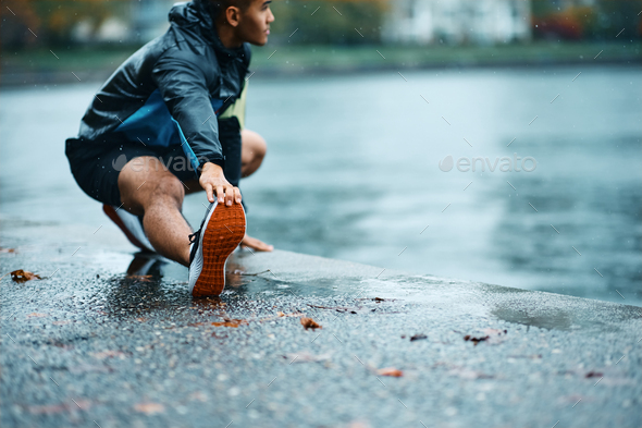 Close up of athlete doing stretching exercises on the road during rainy ...