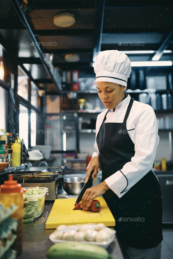 Black female chef chopping food while preparing meal at restaurant ...