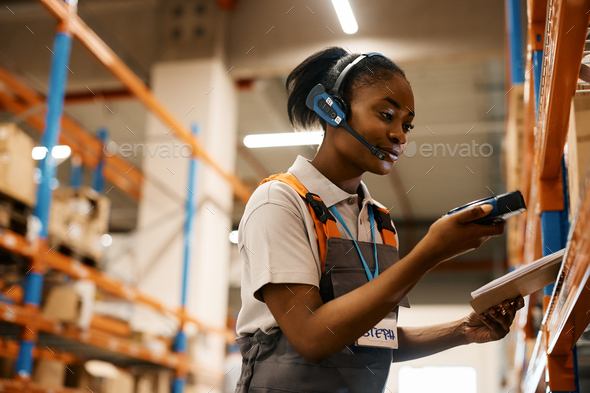 Smiling black warehouse worker scanning labels on packages at ...