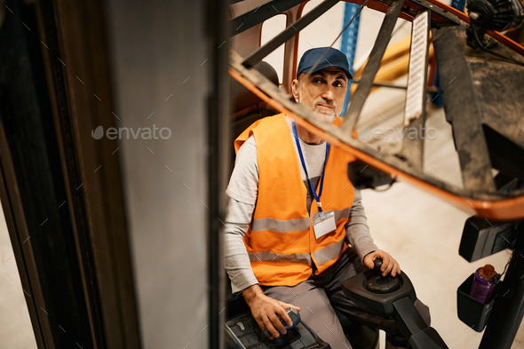 Mature forklift operator loading cargo while working at distribution ...