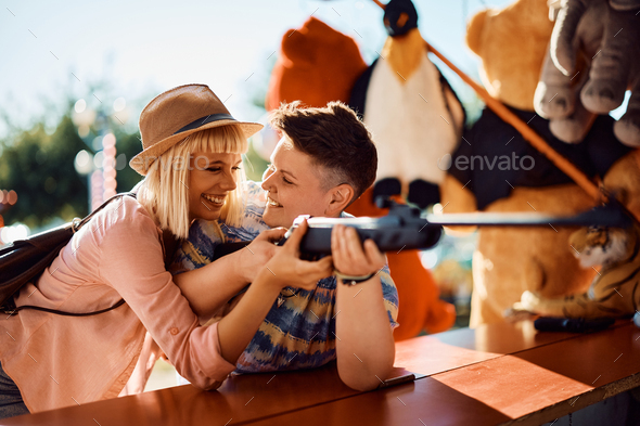 Happy lesbians having fun while aiming at target at carnival booth at ...