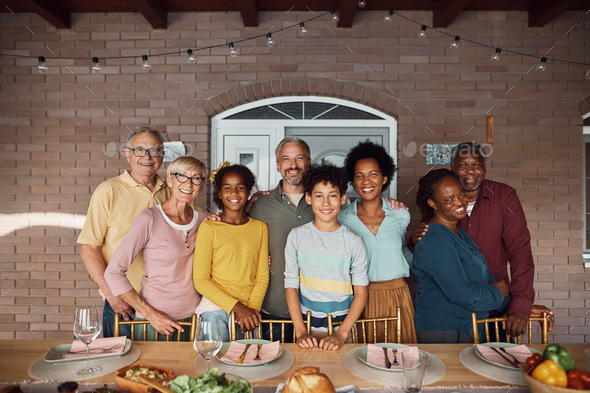 Happy multiracial extended family gathering at dining table on patio ...