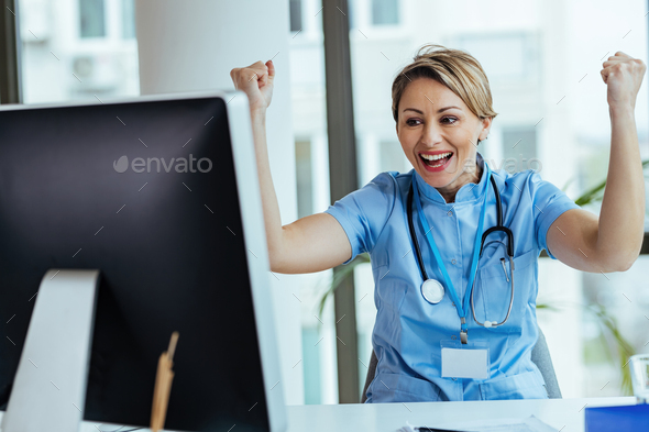 Happy female doctor celebrating good news while using computer at the ...