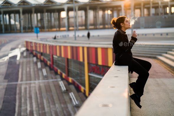 Woman sitting on a railing bridge smoking a cigarette Stock Photo by kikea3