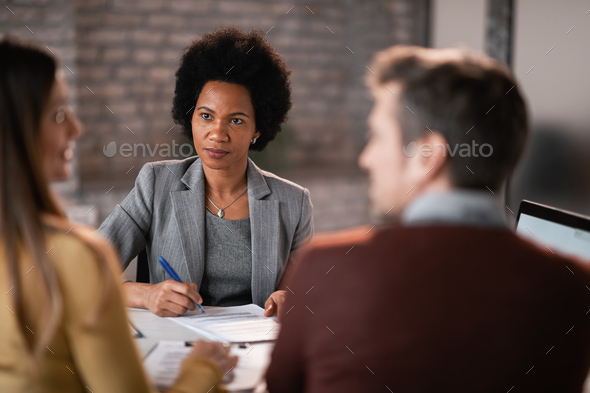 Black female insurance agent taking notes while communicating with a ...