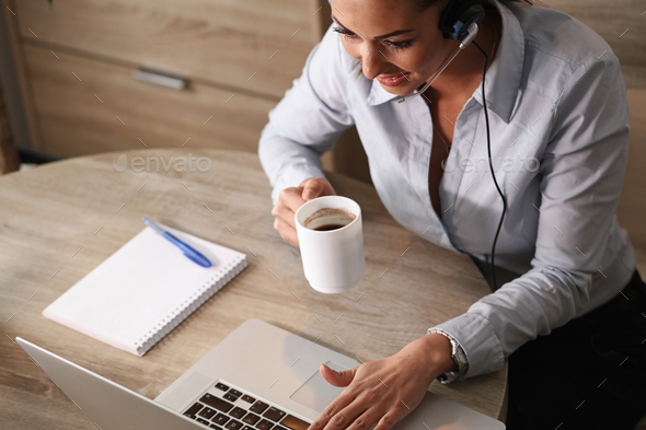 Above view of happy call center agent working on laptop and drinking ...