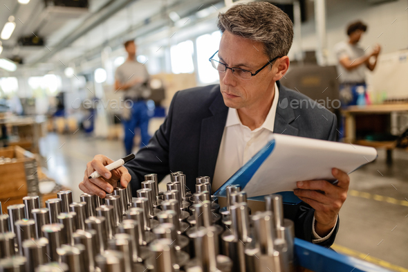 Quality control inspector examining finished steel machine parts in ...