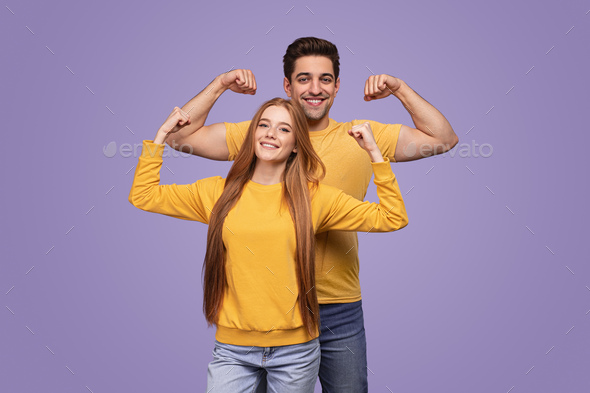 Excited young couple showing biceps in purple studio Stock Photo by kegfire