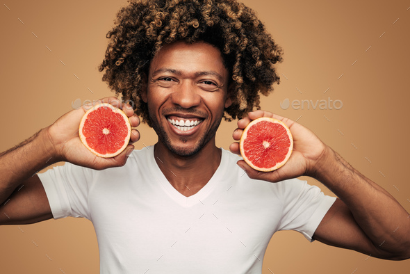 Joyful young black guy showing halved grapefruit in brown studio Stock ...