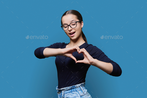 Young smiling female showing heart gesture with fingers, blue ...
