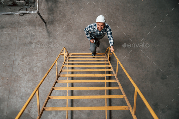 View from the top of ladder. Factory male worker in uniform is indoors ...